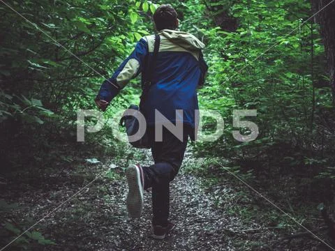 Young scary man running away in the dark forest on the path back view ...